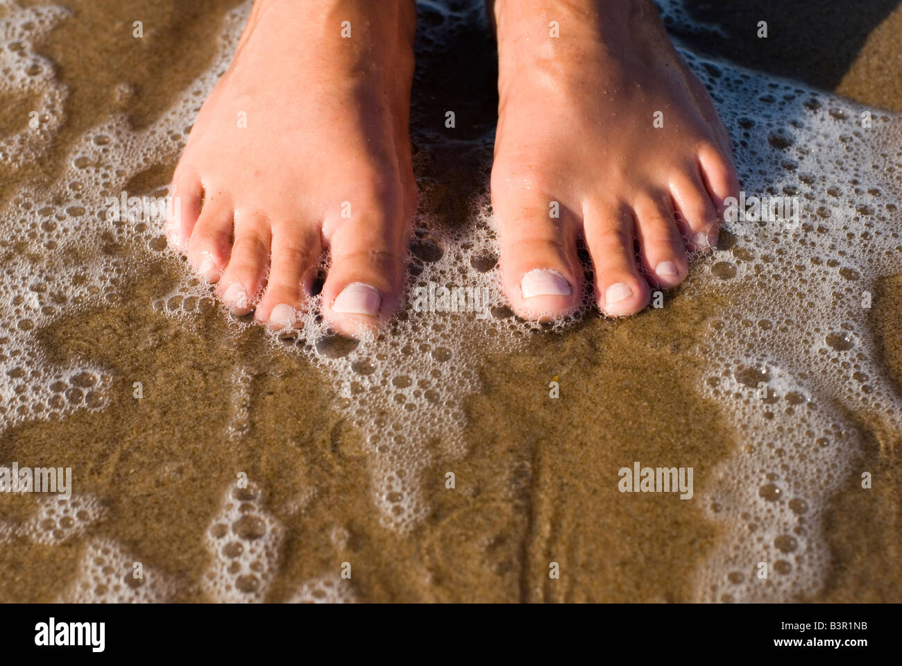 Model Released female feet standing on wet sandy beach with foamy sea ...