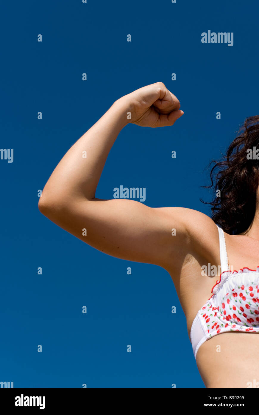 Model Released female arm flexing biceps against a clear blue sky wearing feminine floral bra ...