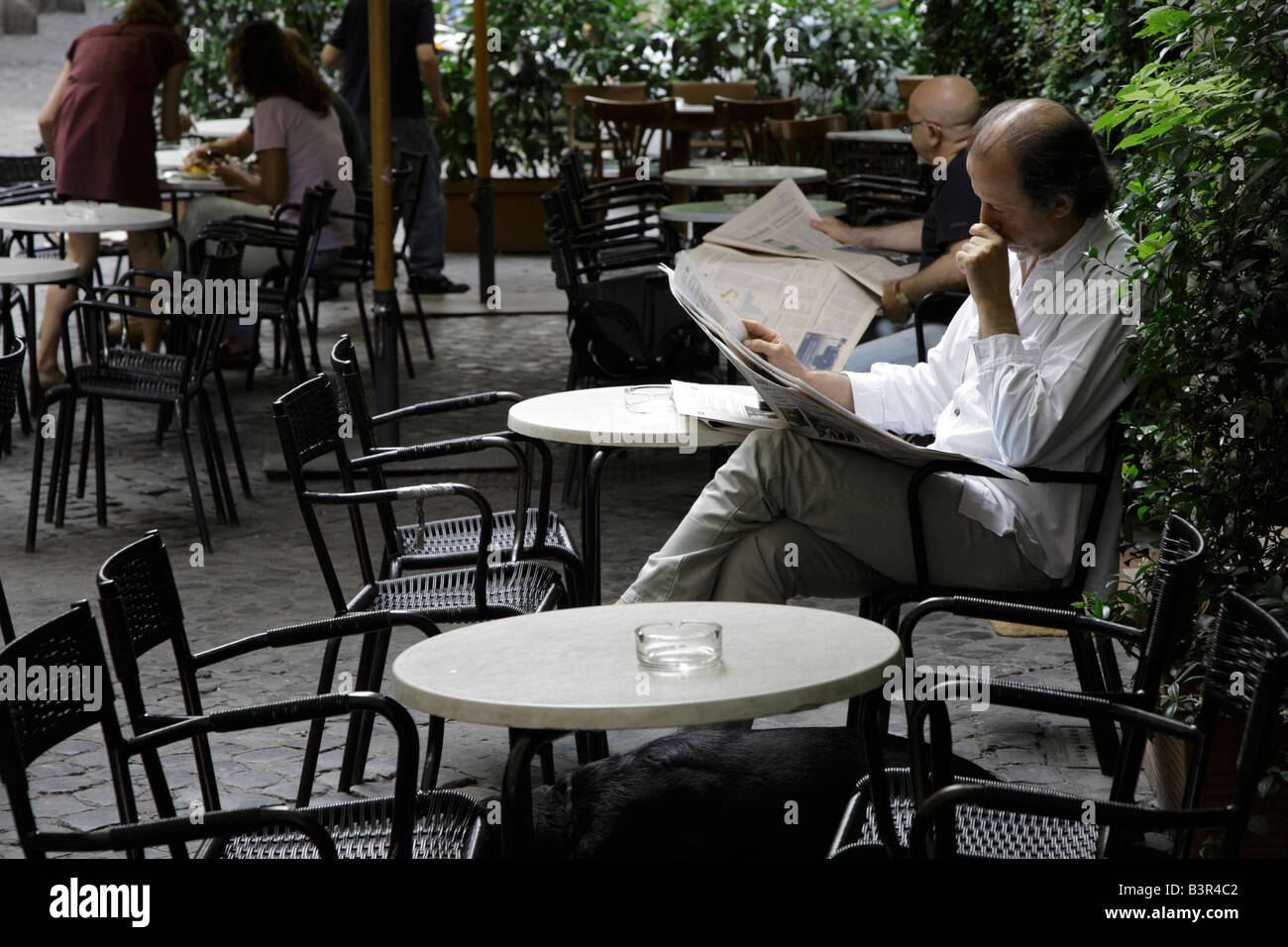 man reading newspaper at street cafe table Stock Photo - Alamy