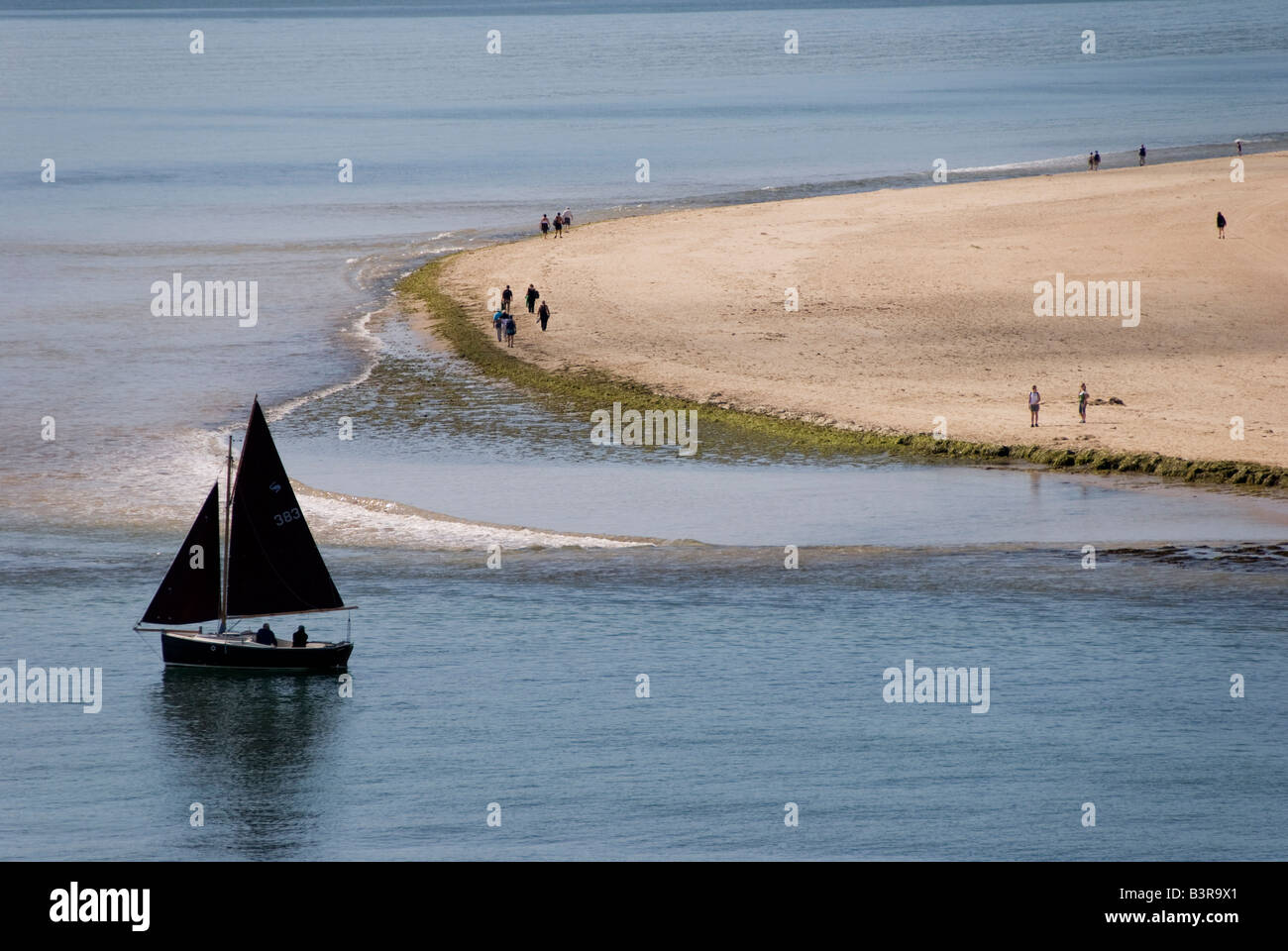 A small sailing boat passes the sandy beach of Shell Bay, Poole, Dorset ...