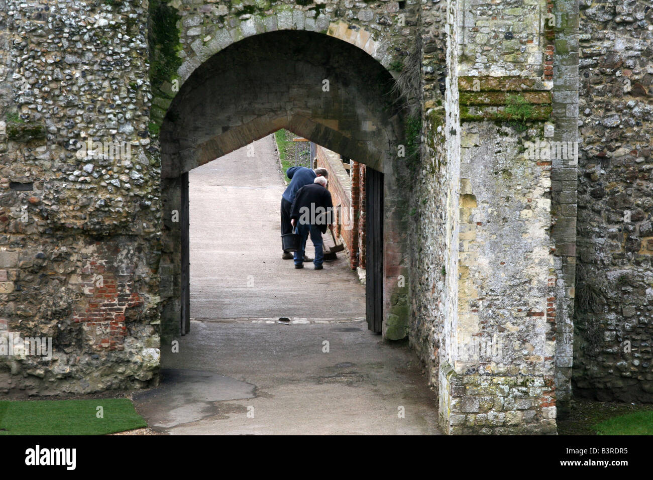 Two men seen through the gateway of Framlingham Castle sweep up Stock ...