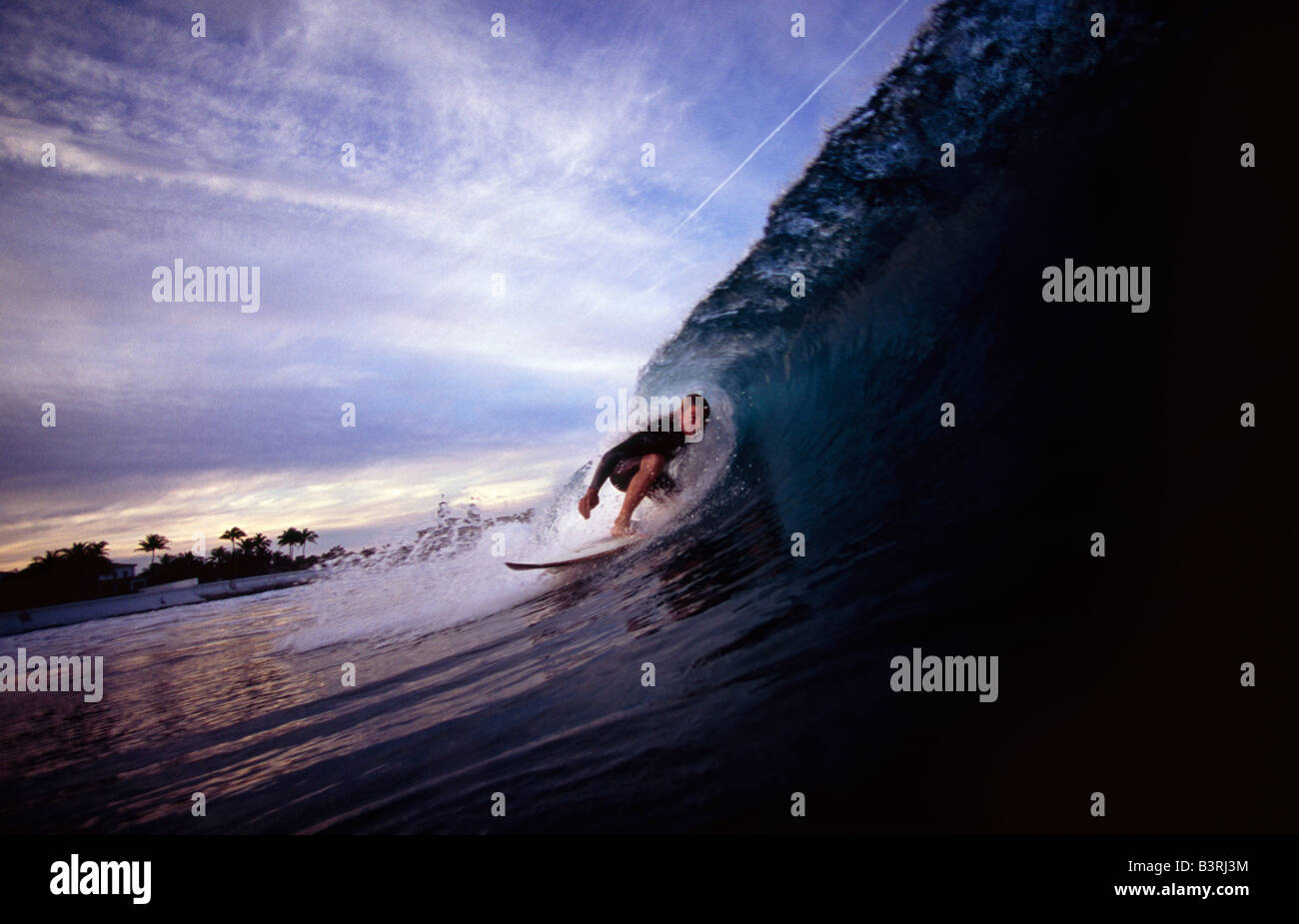 Surfer underneath the curl of a wave in the late in the afternoon off ...