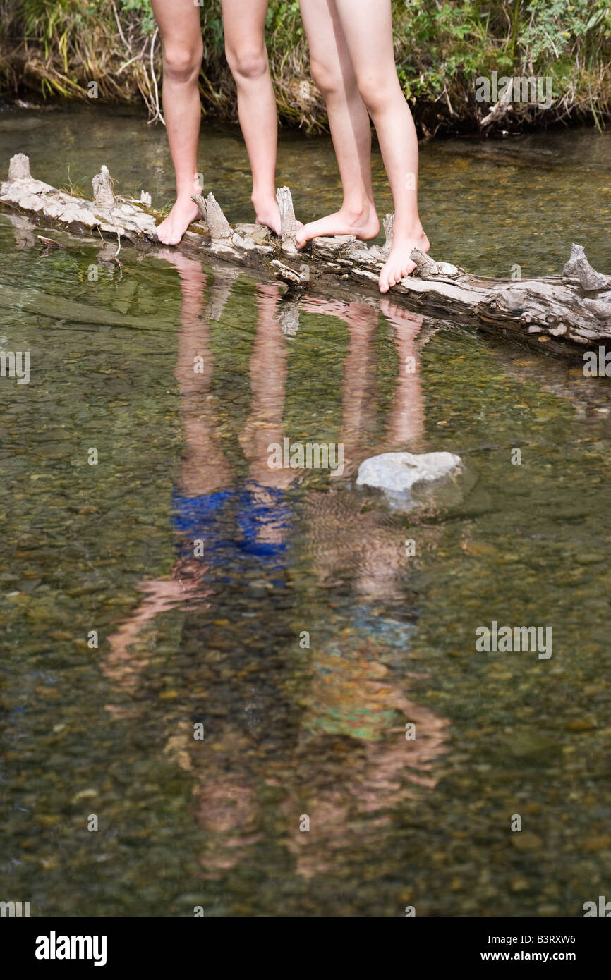 Two girls standing on log in stream Stock Photo - Alamy