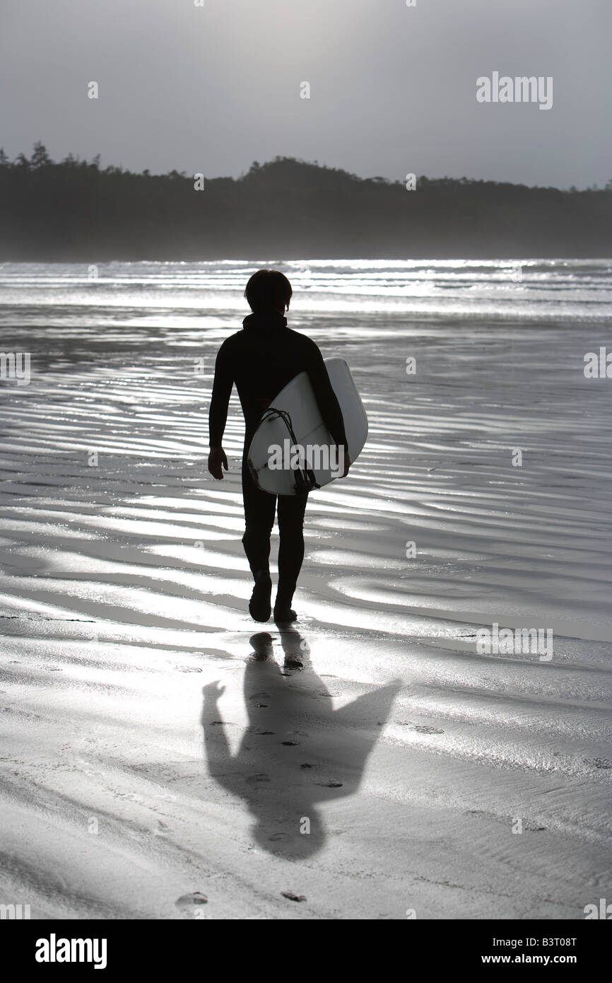 Cox Bay, Tofino, British Columbia, Canada; Surfer walking on the beach ...