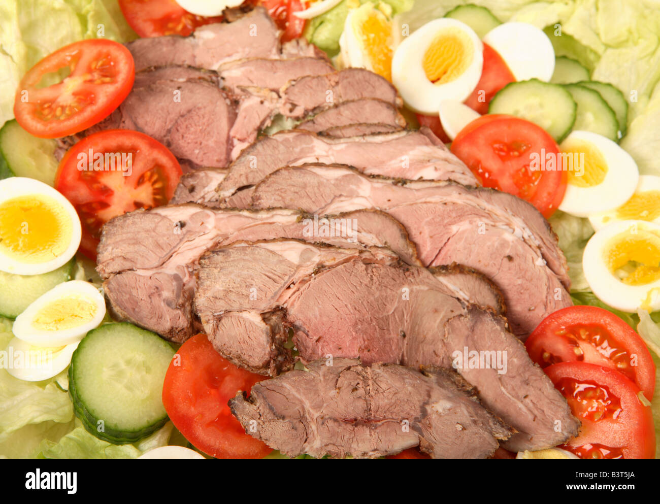 A display of slices of cold roast lamb with egg tomato cucumber and ...