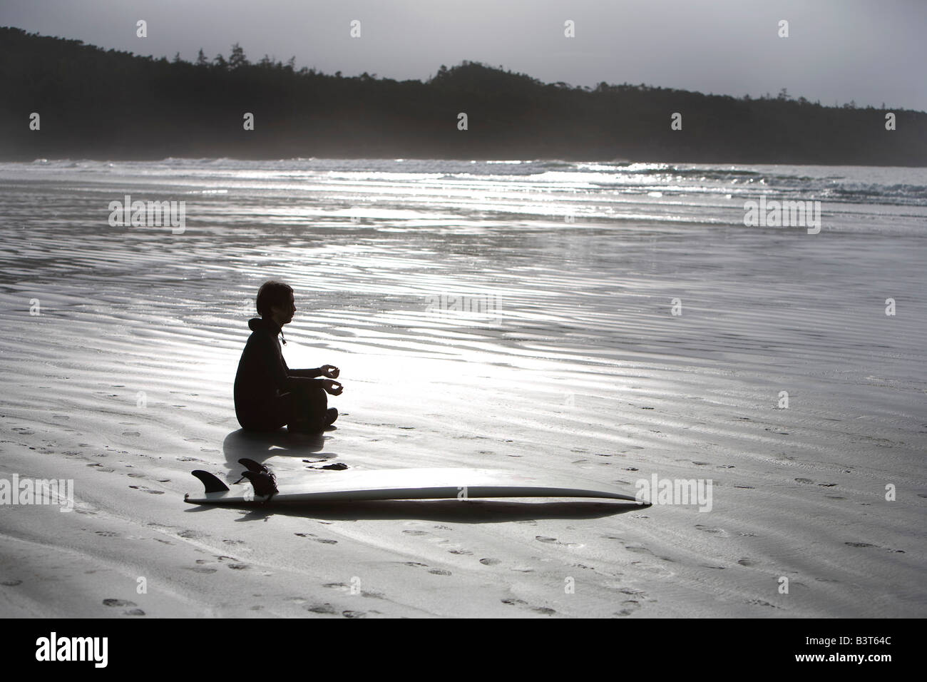 Surfer meditating on beach, Cox Bay near Tofino, British Columbia ...