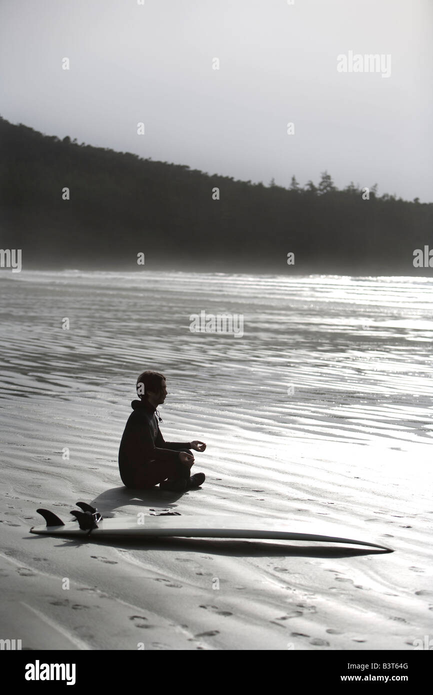 Surfer meditating on beach, Cox Bay near Tofino, British Columbia ...