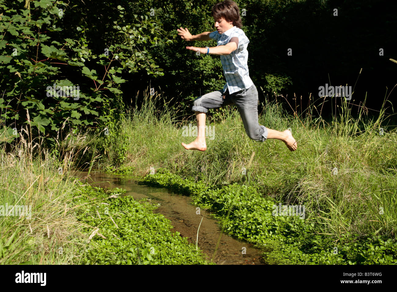 teenage boy jumping across a stream Stock Photo - Alamy