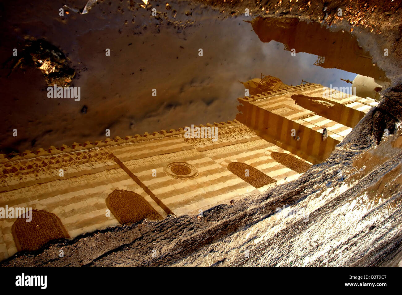 Reflection of a stone mosque, and its fine carvings, in a pool of water ...