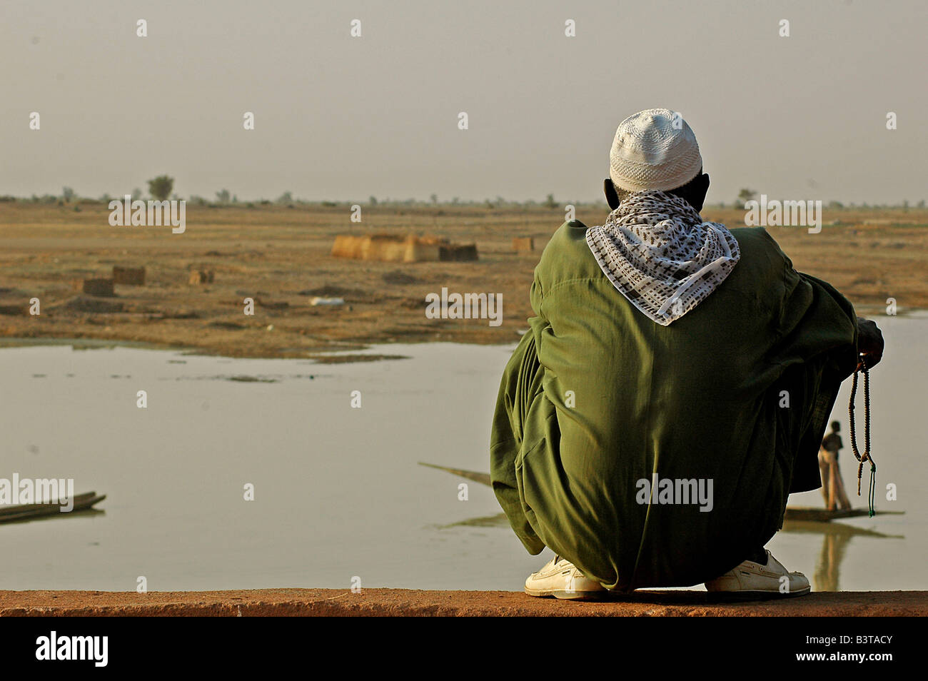 Squatting muslim man holding a prayer chaplet watching the Niger river ...