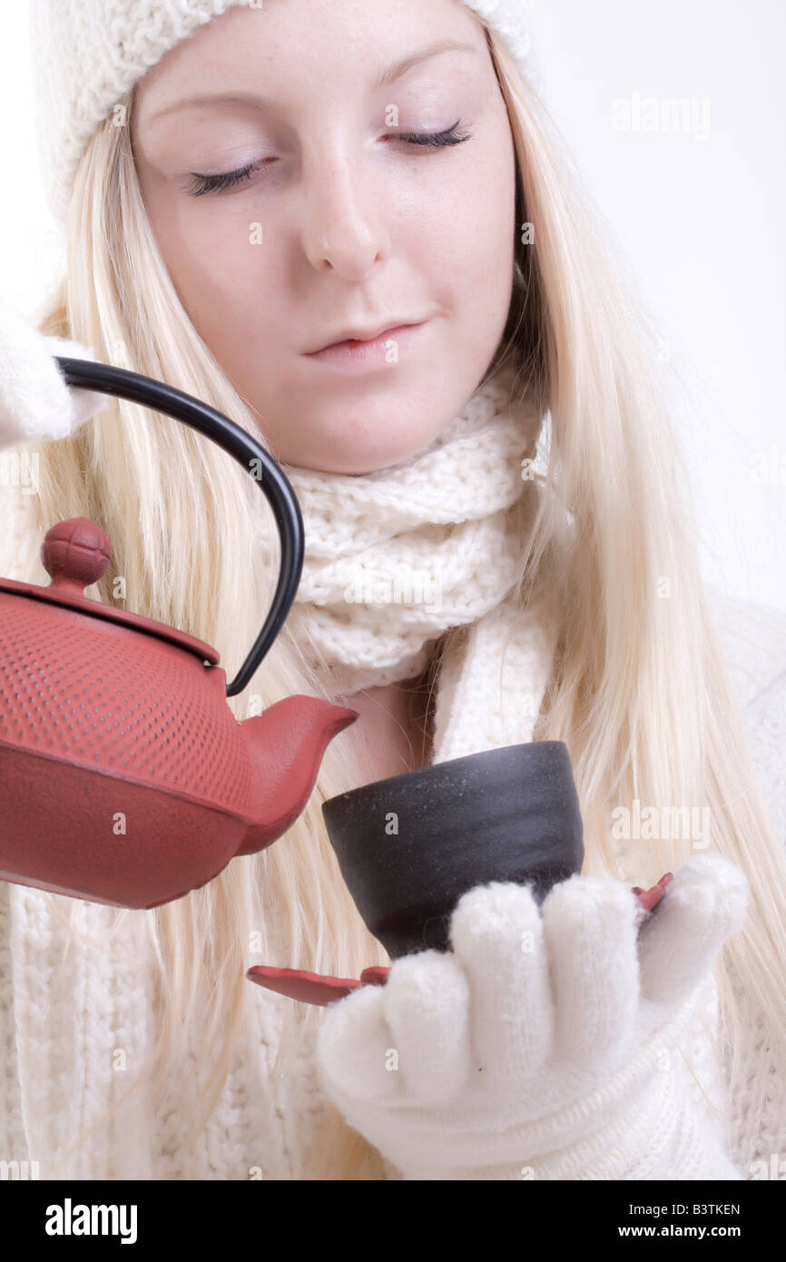 young woman in white winter clothes pouring tea from teapot into tea ...