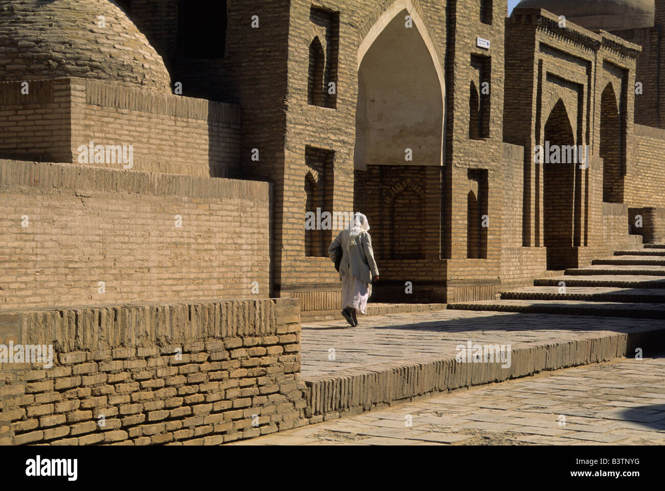 Uzbek woman walking by old inner town buildings, Khiva, Uzbekistan ...