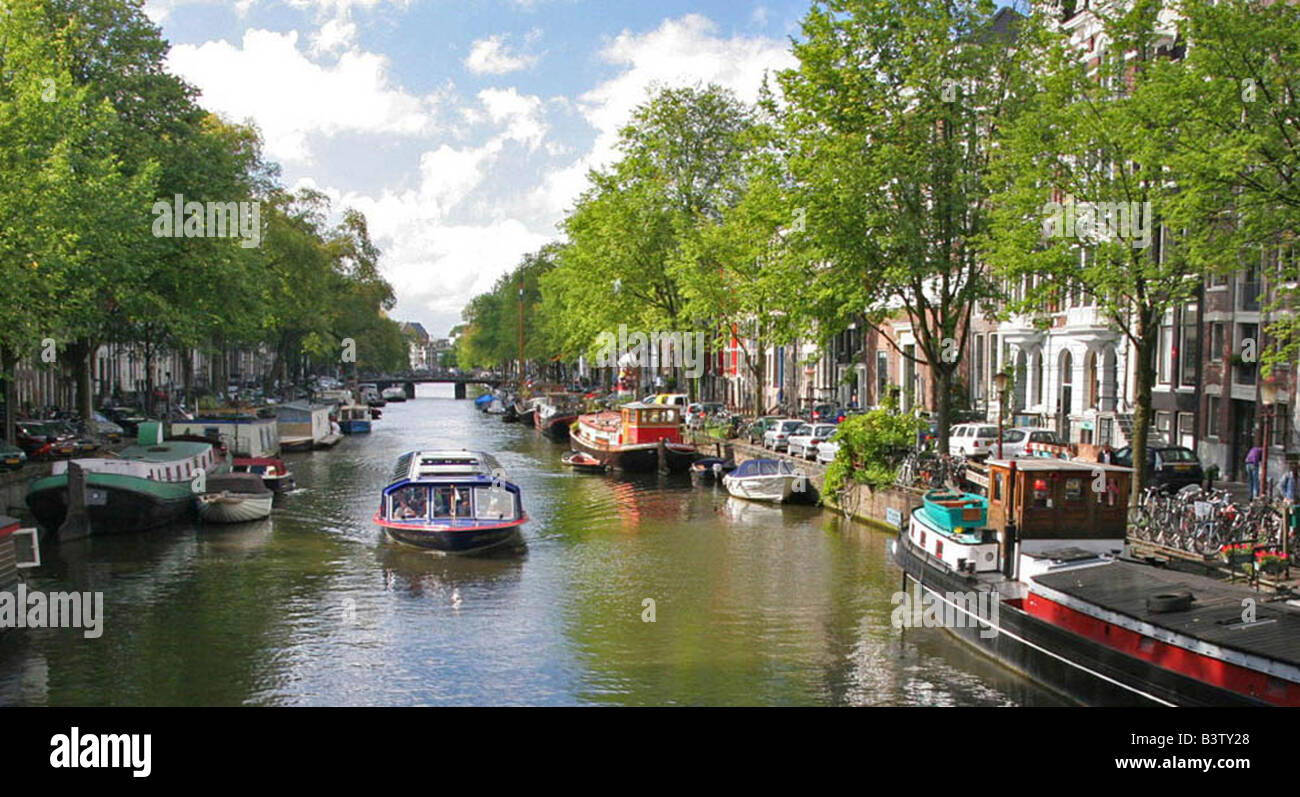 A tour boat passes many colorful houseboats on a tree lined canal Stock ...