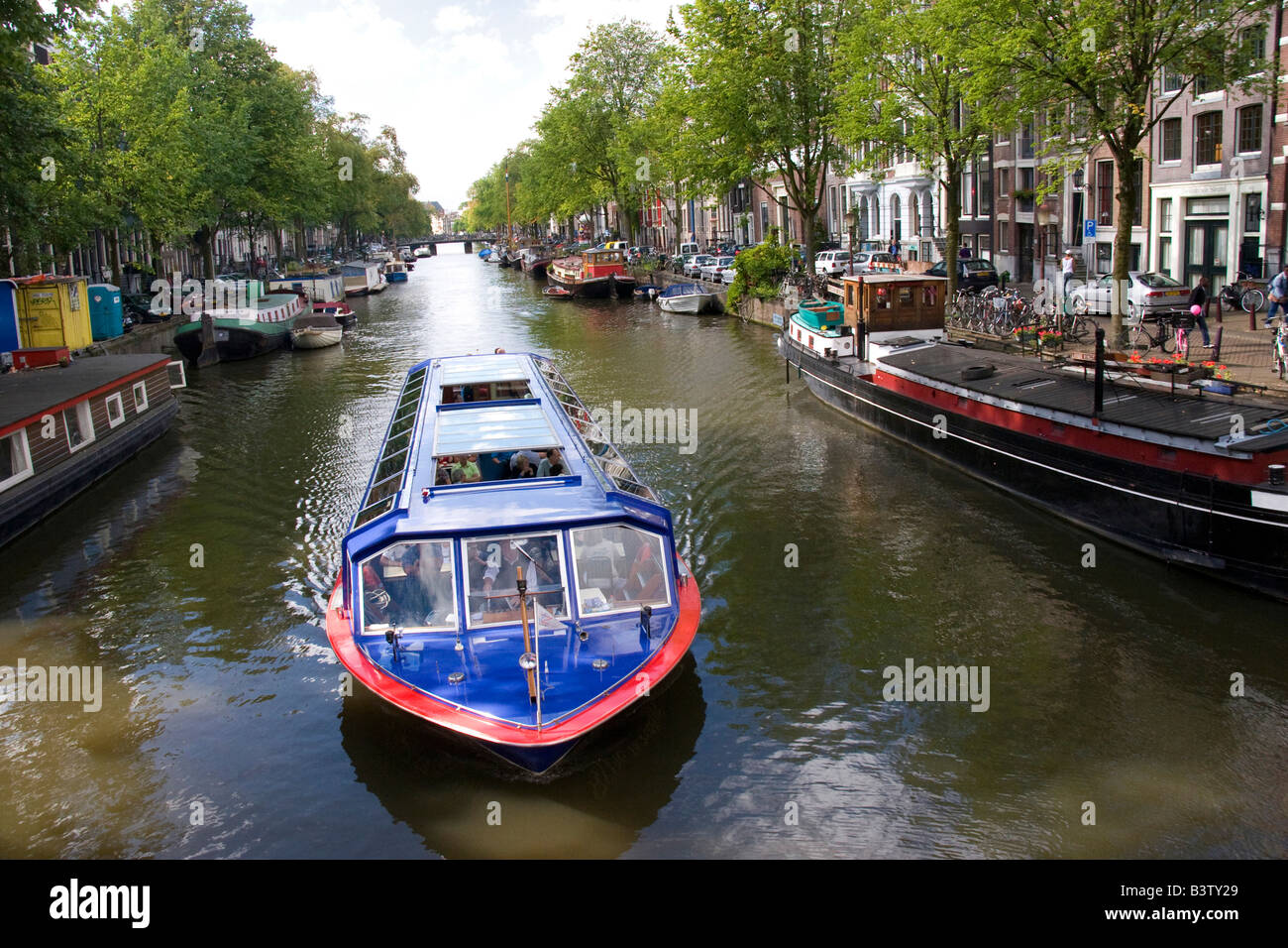 A boat full of tourist travel a canal lined with trees and colorful ...