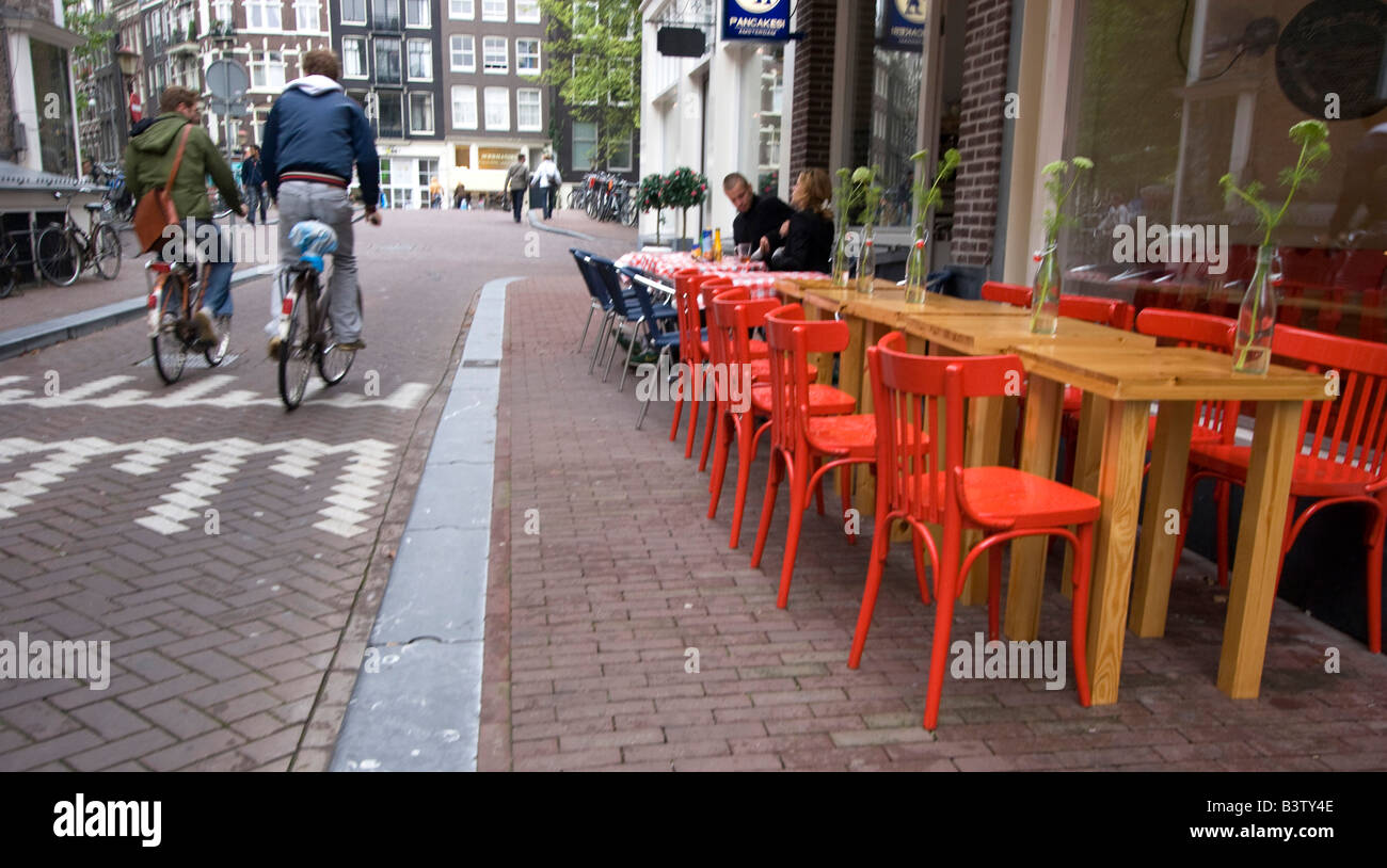 Busy street scene withpeople riding bikes past a colorful outdoor cafe ...