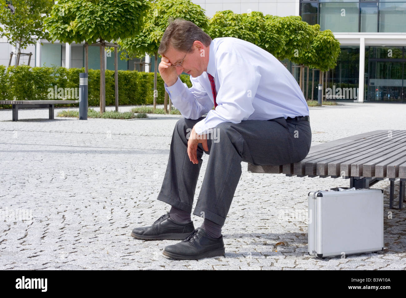 Sorrowful businessman sitting on a bench in front of an office building ...