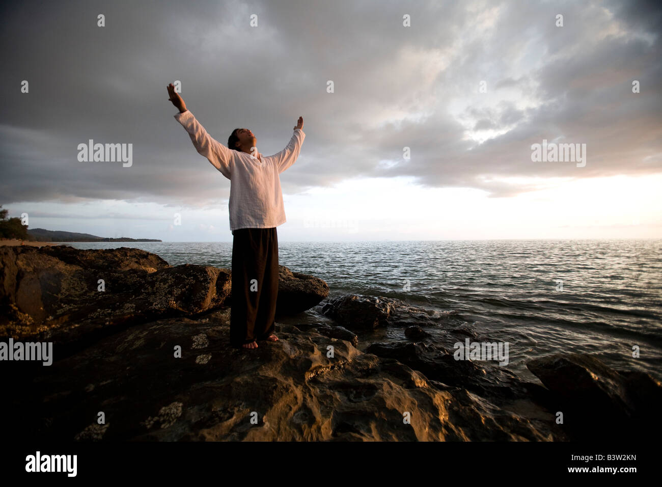 A person with arms raised on a beach at sunset, Koh Lanta, Thailand ...