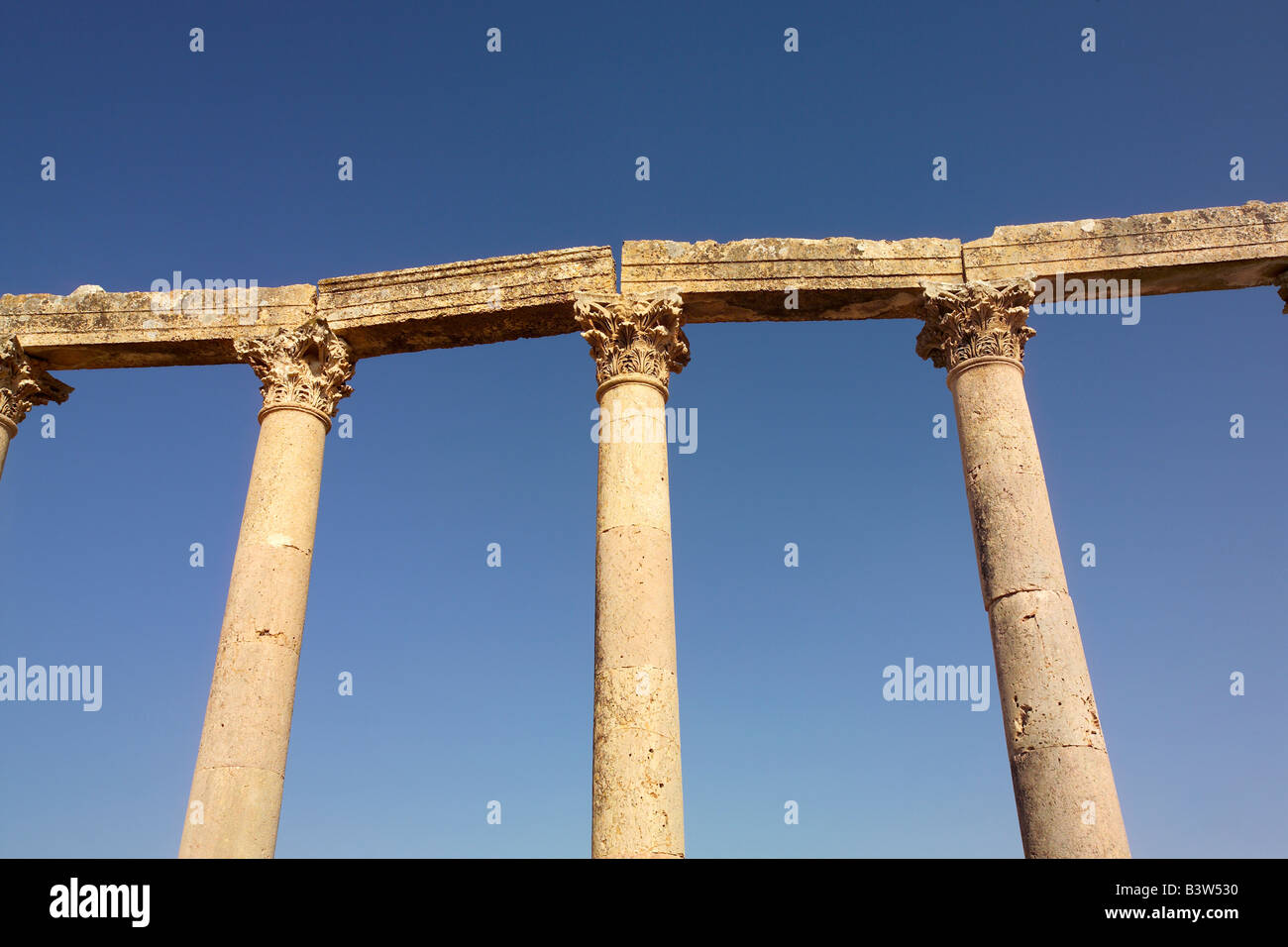 Looking up at three ancient Roman columns joined together by beams of ...