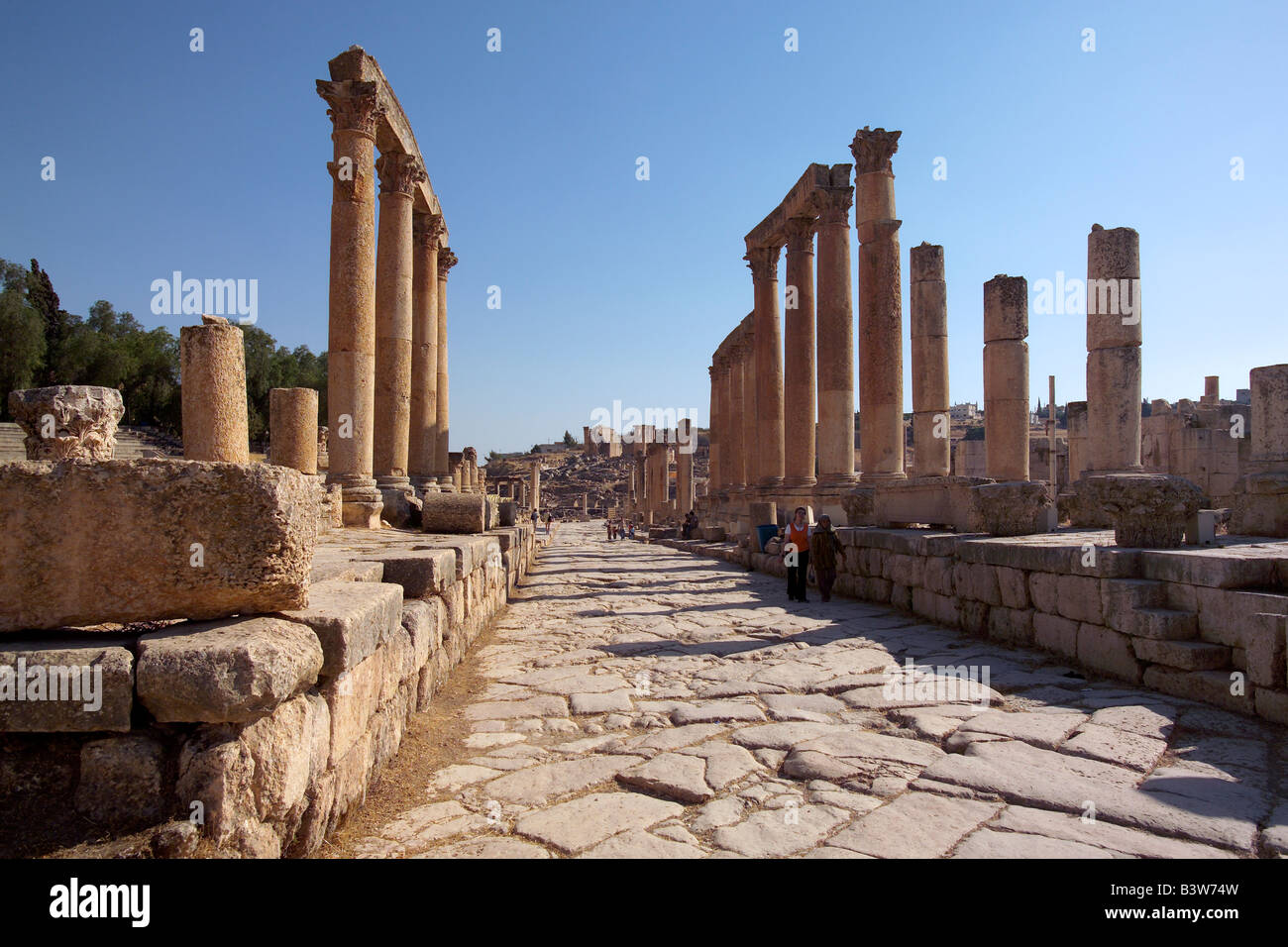 Huge slabs of stone form a well worn pavement. Either side are ruins of ...