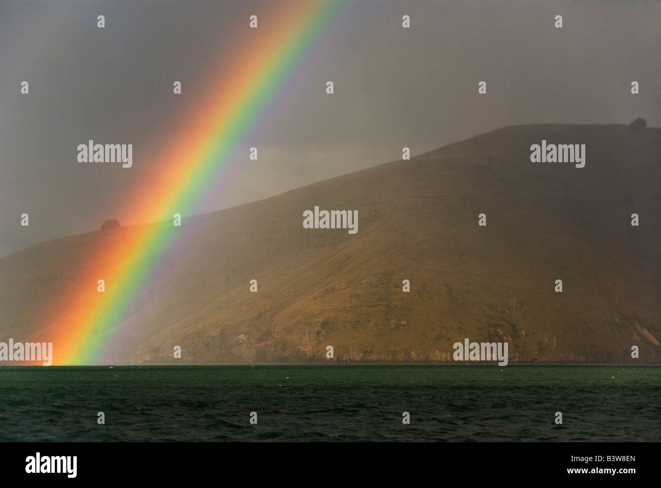 Rainbow dropping into the sea against a background of coastal hills ...