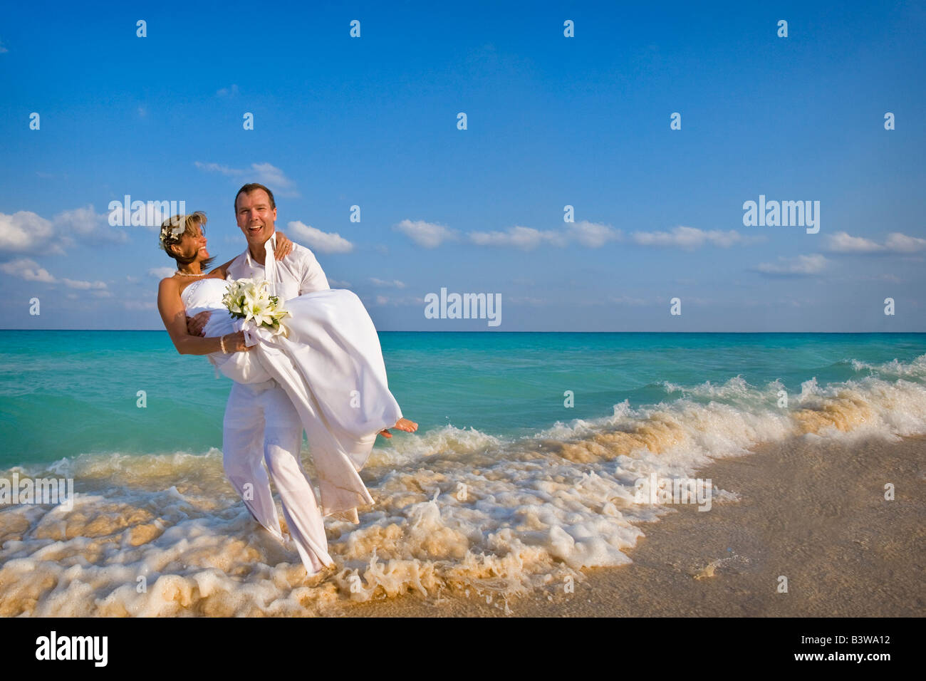 Groom carrying bride on beach Stock Photo - Alamy
