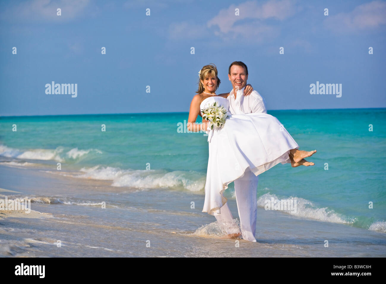 Groom carrying bride on beach Stock Photo - Alamy