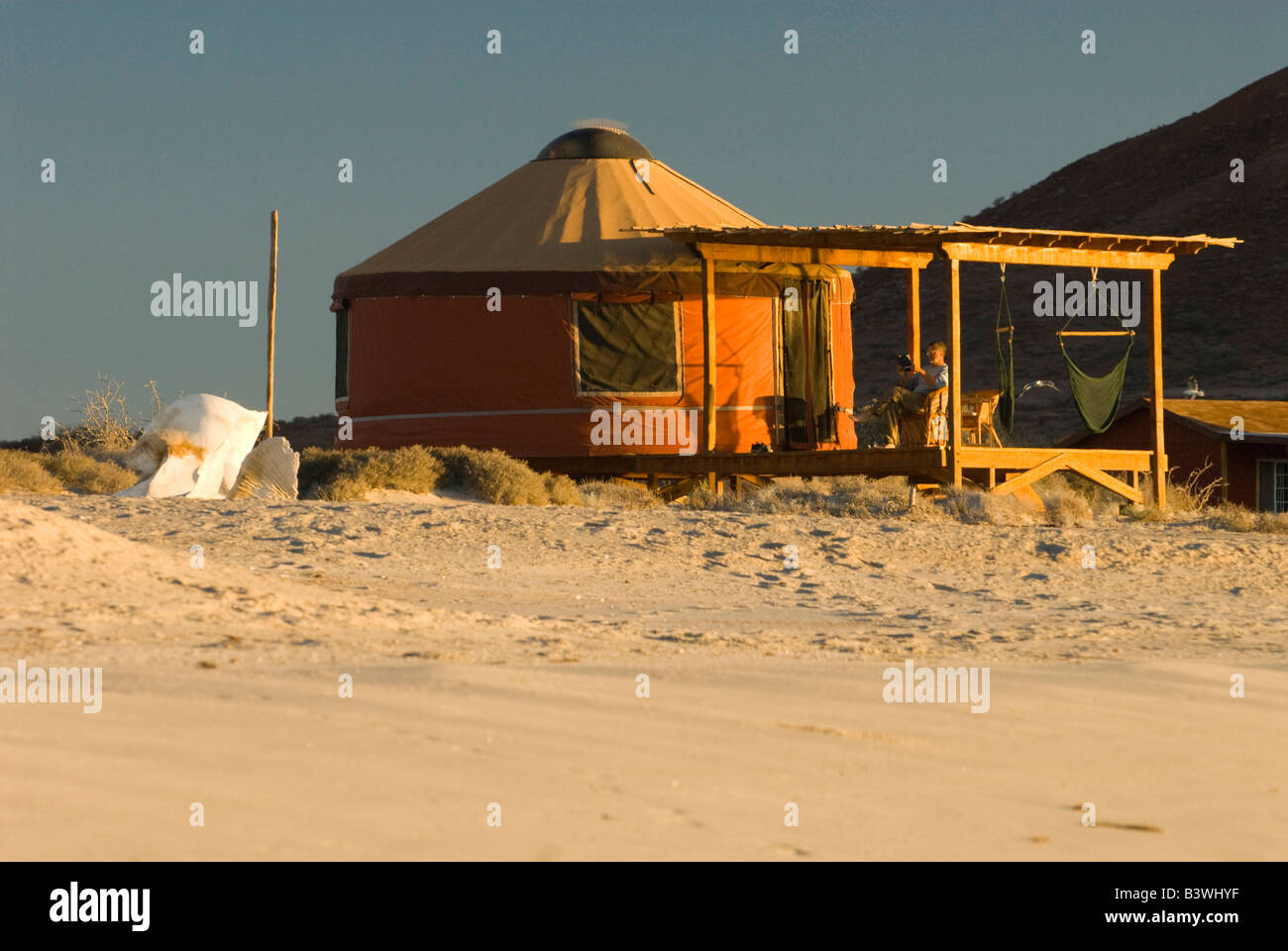 Mexico, Baja California, Bahia de las Animas. Man reads on porch of ...