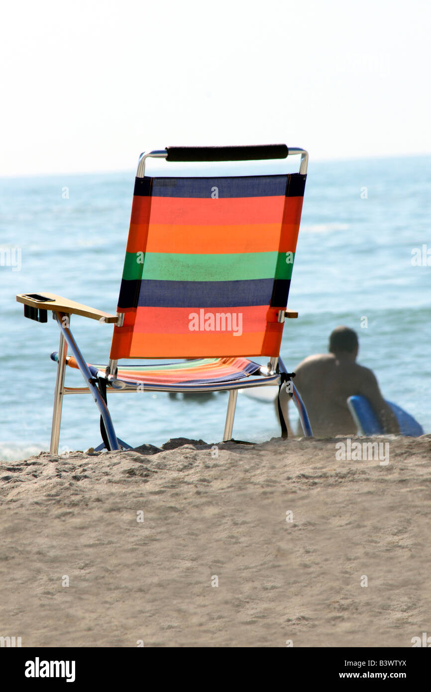 Deck chair on the beach with a man carrying a surfboard in the ...