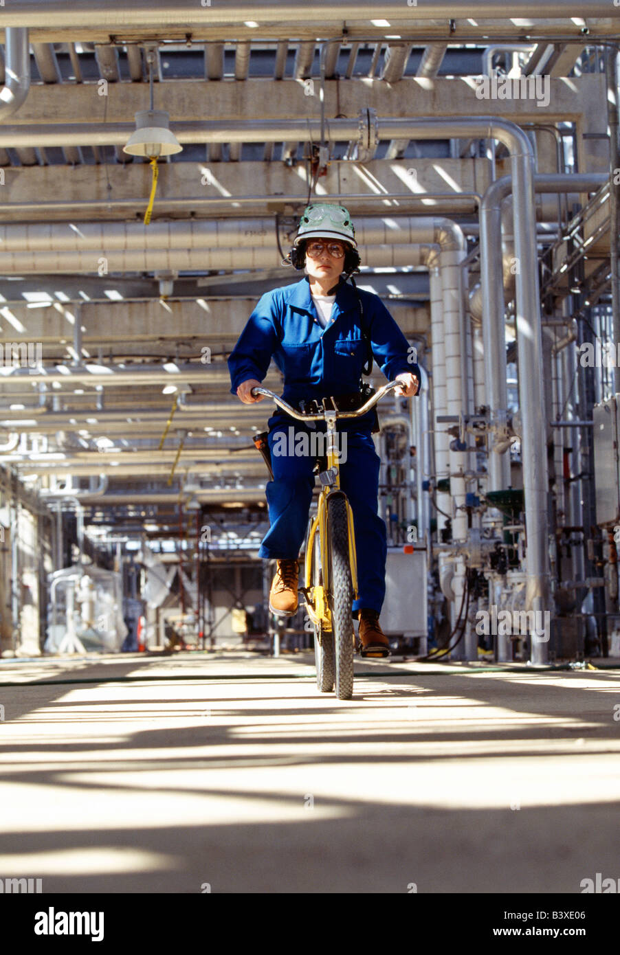 Female worker in overalls rides a bike through a large refinery in ...