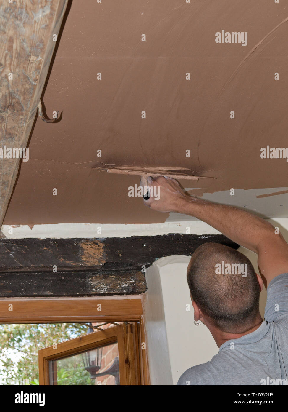 PLASTERER USING TROWEL TO APPLY FIRST COAT OF MIXED PLASTER TO ...