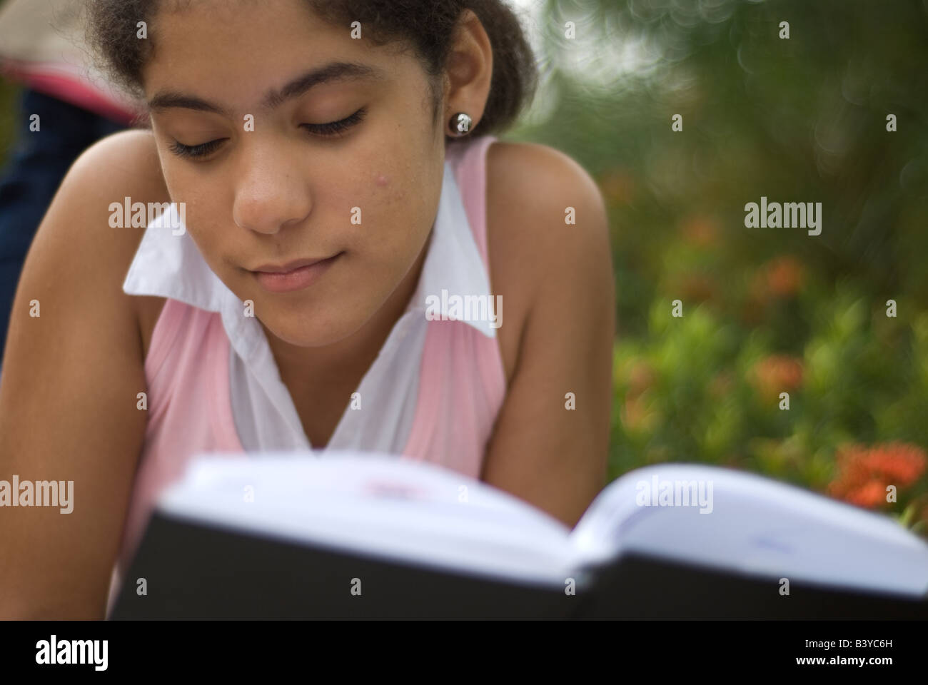 A young Latina teenager reading a black book while laying down on a ...
