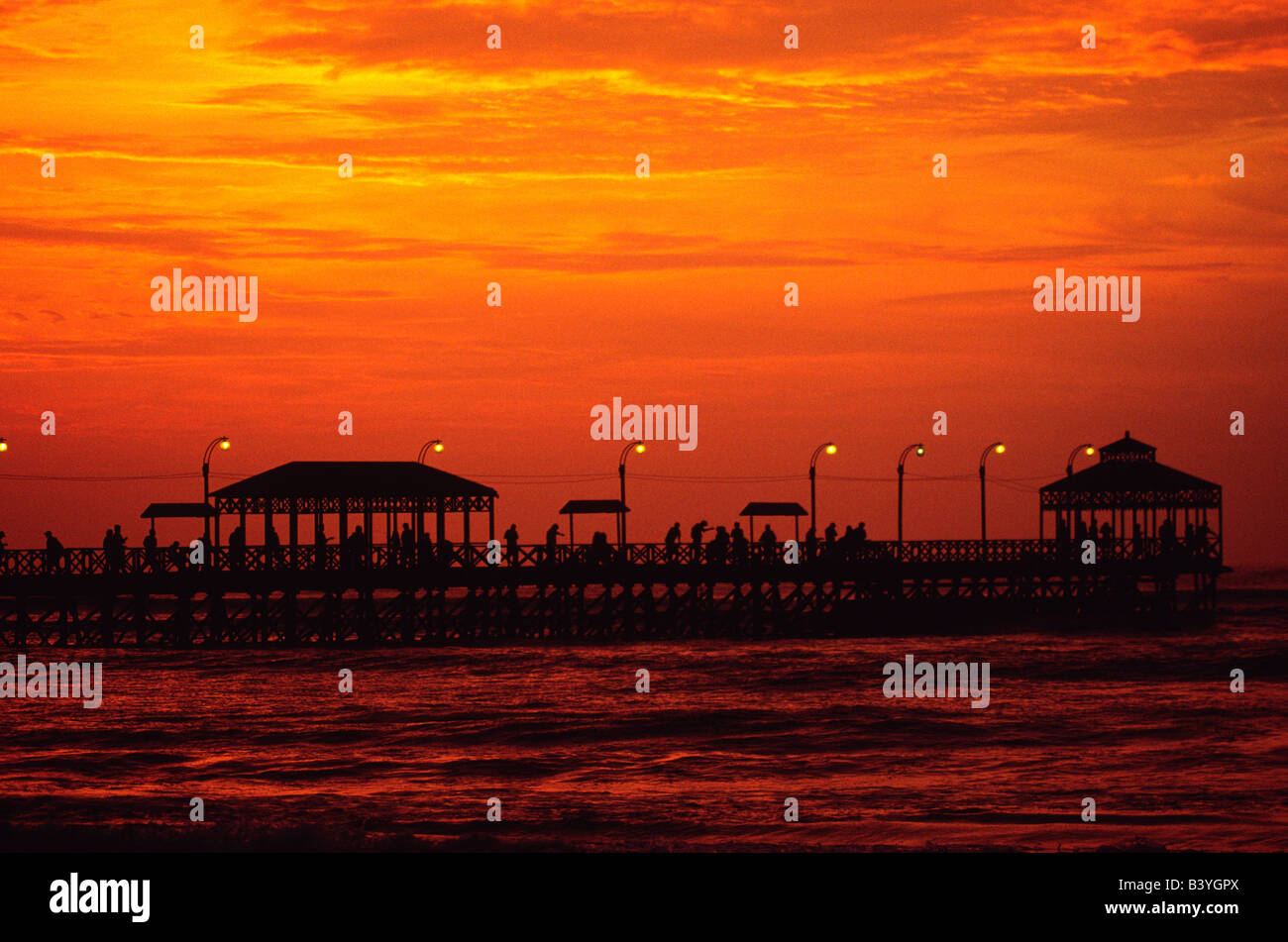 Peru, La Libertad, The sun sets over the Pacific, silhouetting figures ...