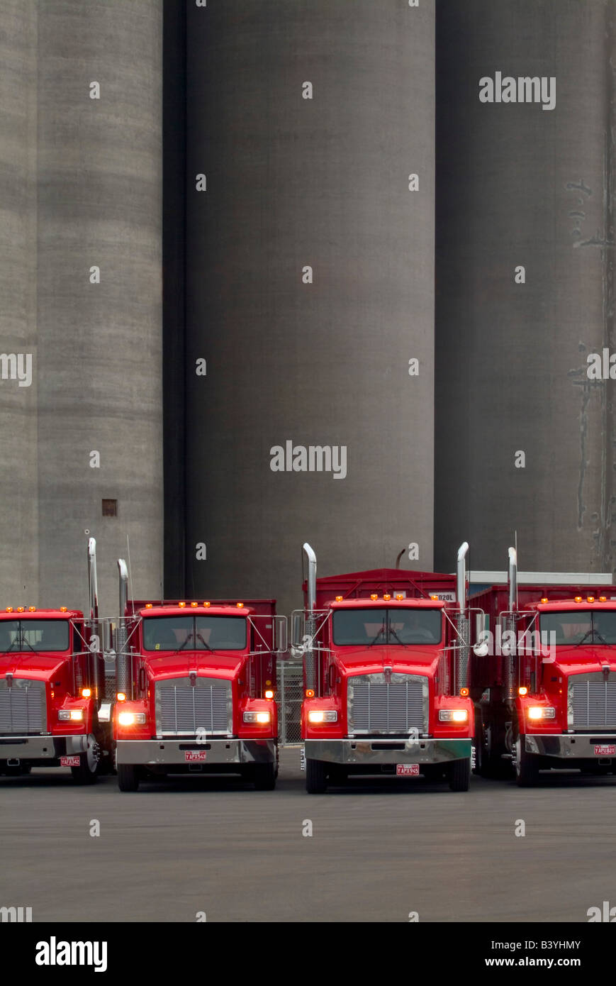 Four red trucks with lights turned on lined up in front of tall ...
