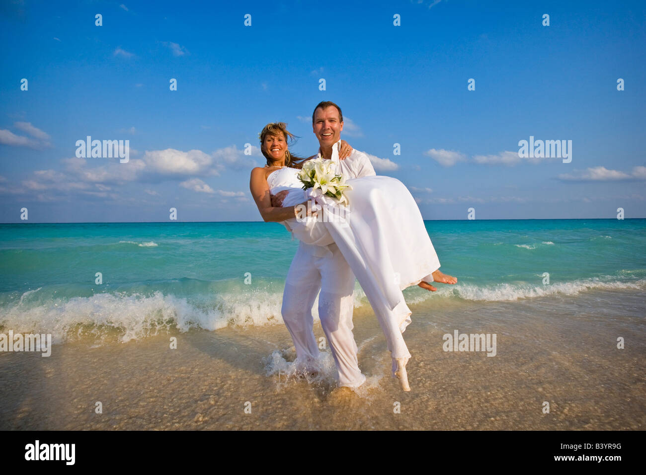 Groom carrying bride on beach Stock Photo - Alamy
