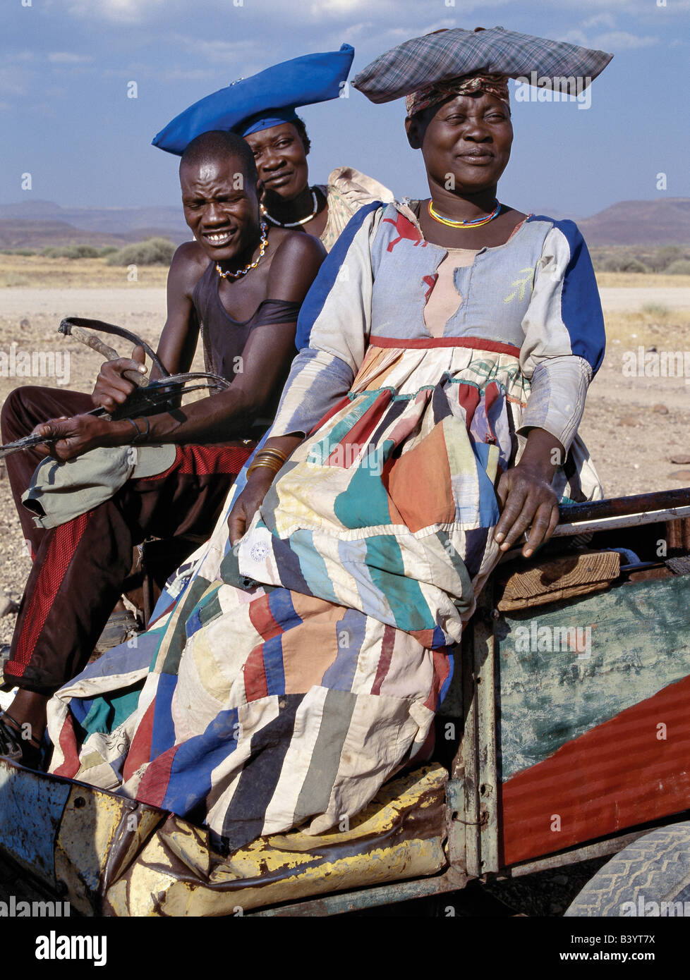 Namibia, Damaraland, Palmwag. An Herero man and two women ride home in ...