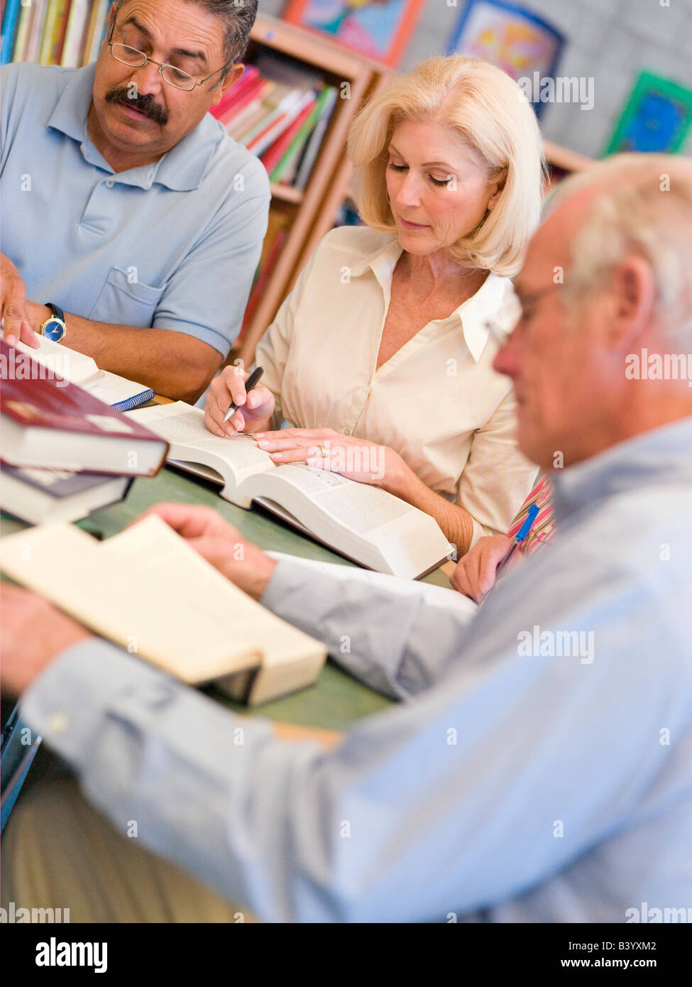 Three people sitting in library with books and notepads (selective ...