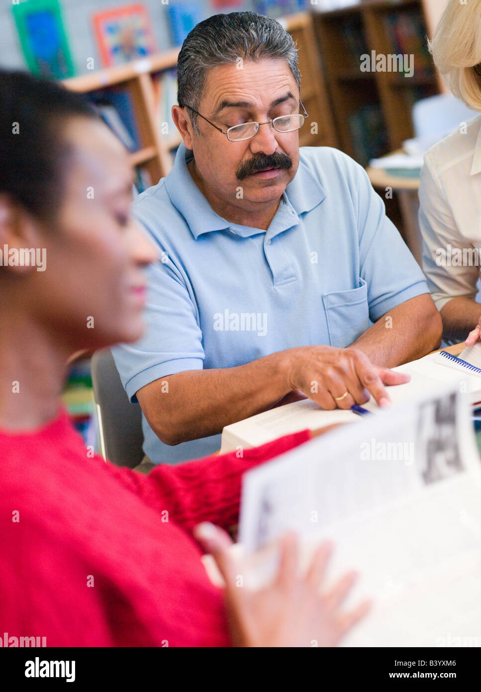 Three people sitting in library with books and notepads (selective ...