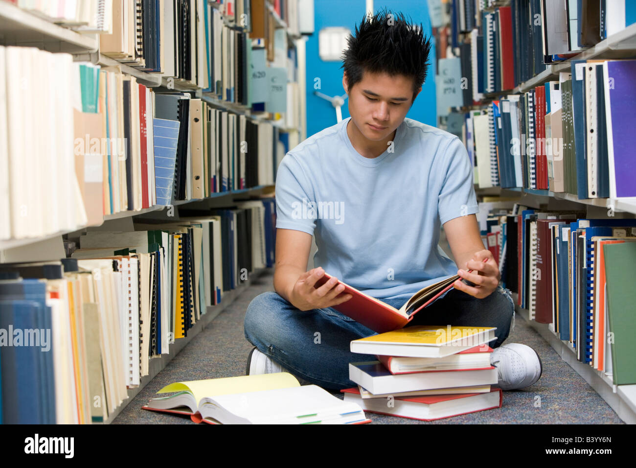 Man sitting on floor in library reading book Stock Photo - Alamy