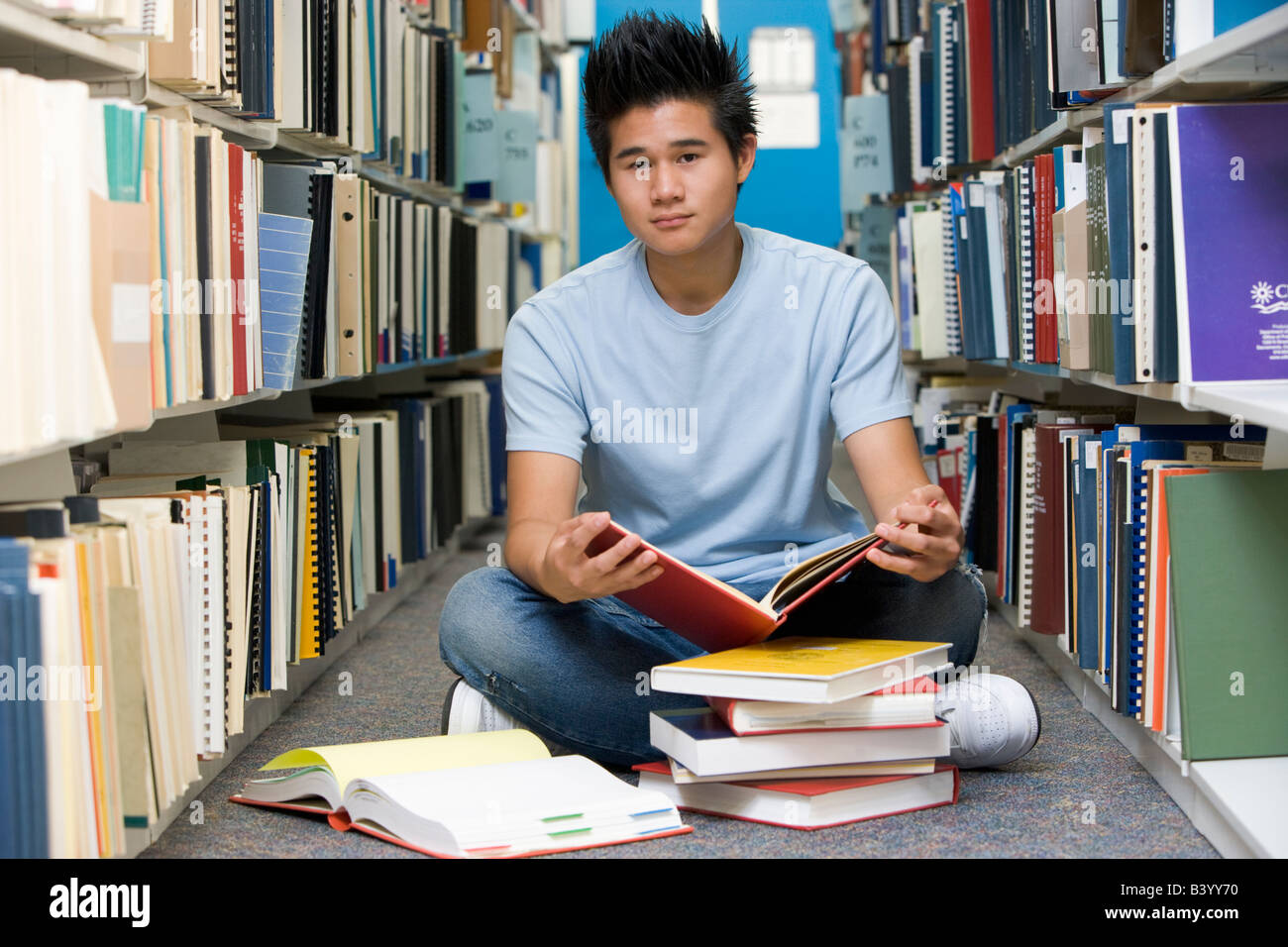 Man sitting on floor in library holding book Stock Photo - Alamy