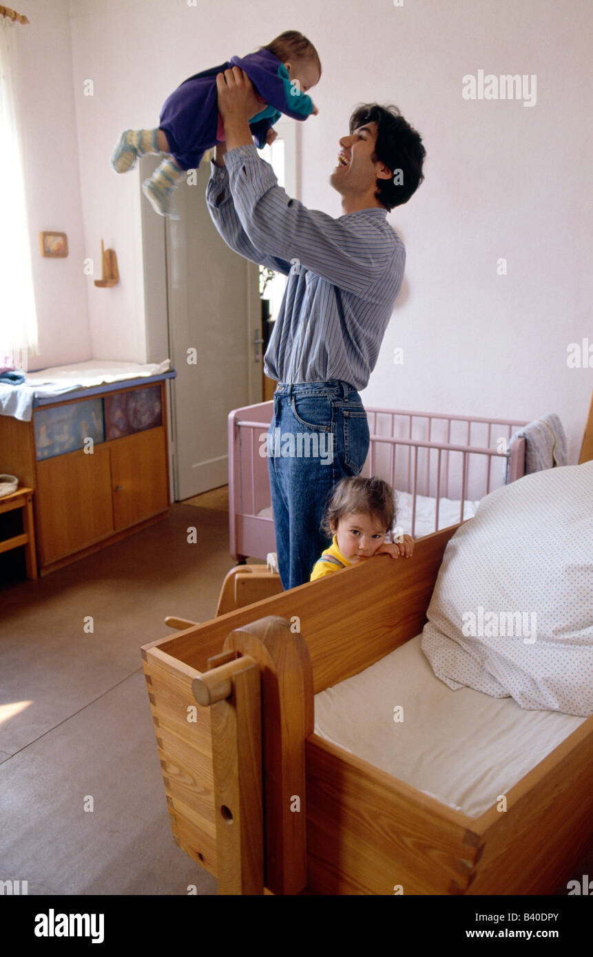 German father playing with his infant son while his daughter eyes the ...