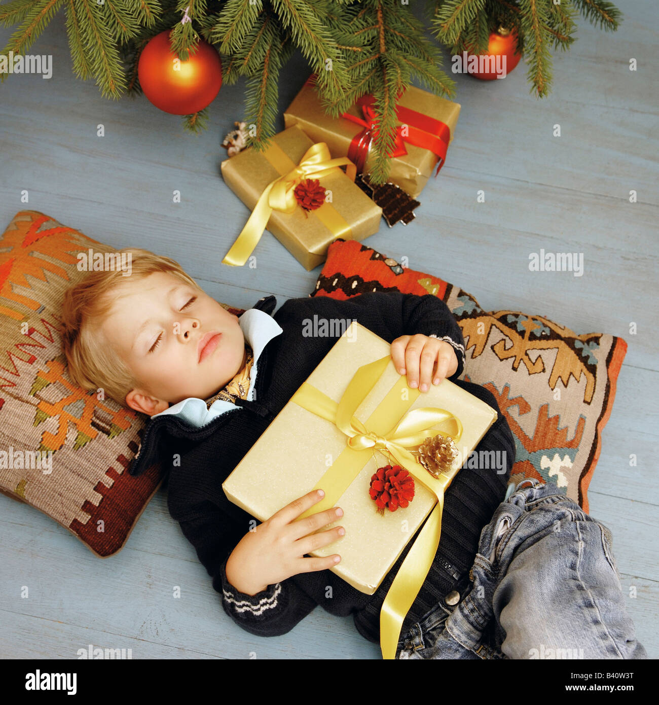 Boy (5-6 years) holding gift sleeping under a Christmas tree Stock ...