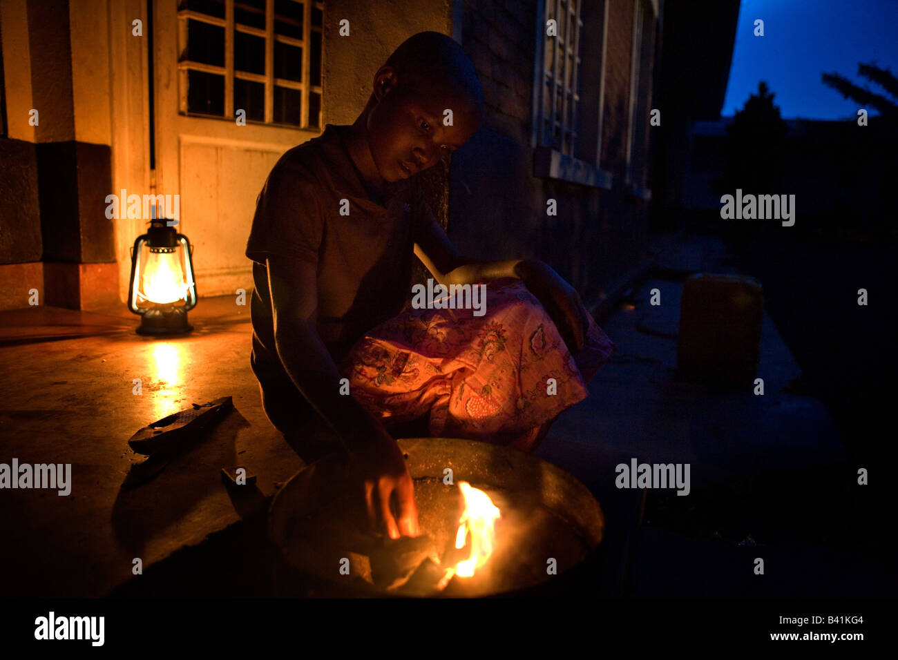 A young Rwandan girl stokes the fire in preparation for cooking dinner ...