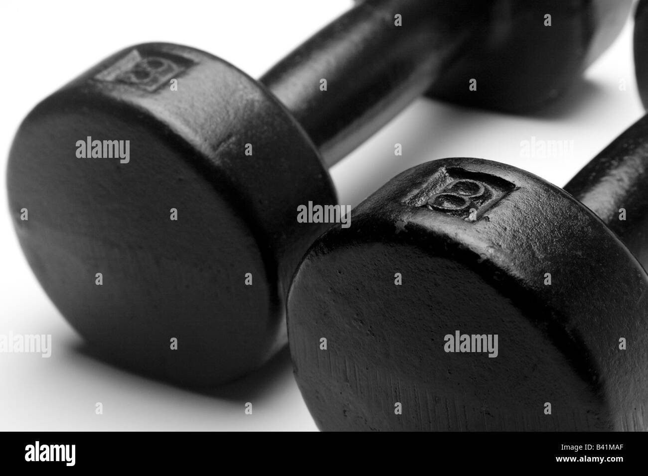 Partial view of two black exercise hand barbells, weights, stamped with ...