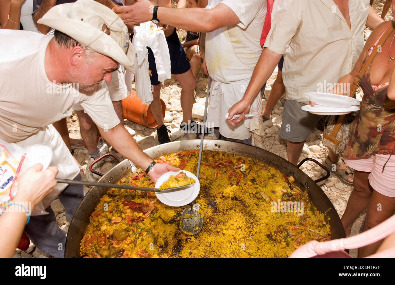 portions of a giant Paella are being dished out to hungry eaters in ...