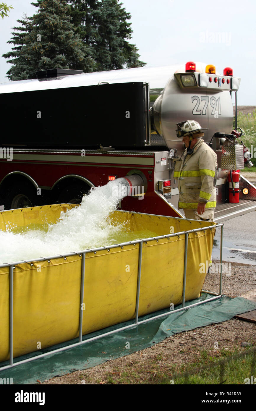 A tanker filling a canvas holder with water at a rural emergency fire ...
