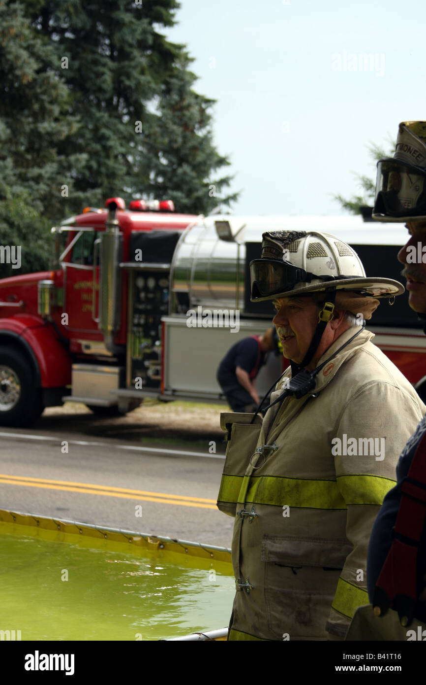 Firefighter personnel standing at a fire scene with a tanker in the ...