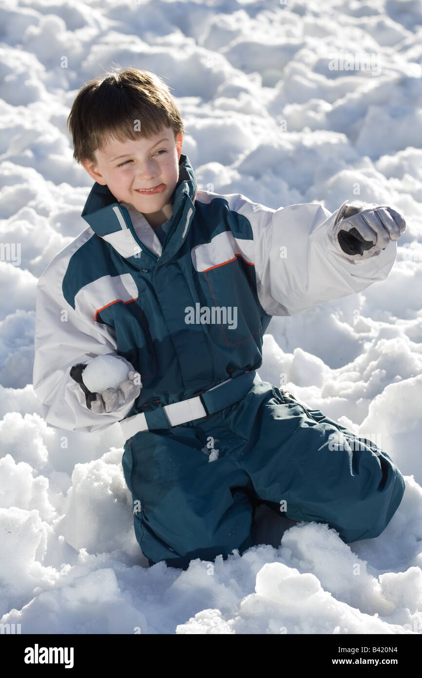 Portrait of a boy preparing to throw a snowball. He is wearing a white ...