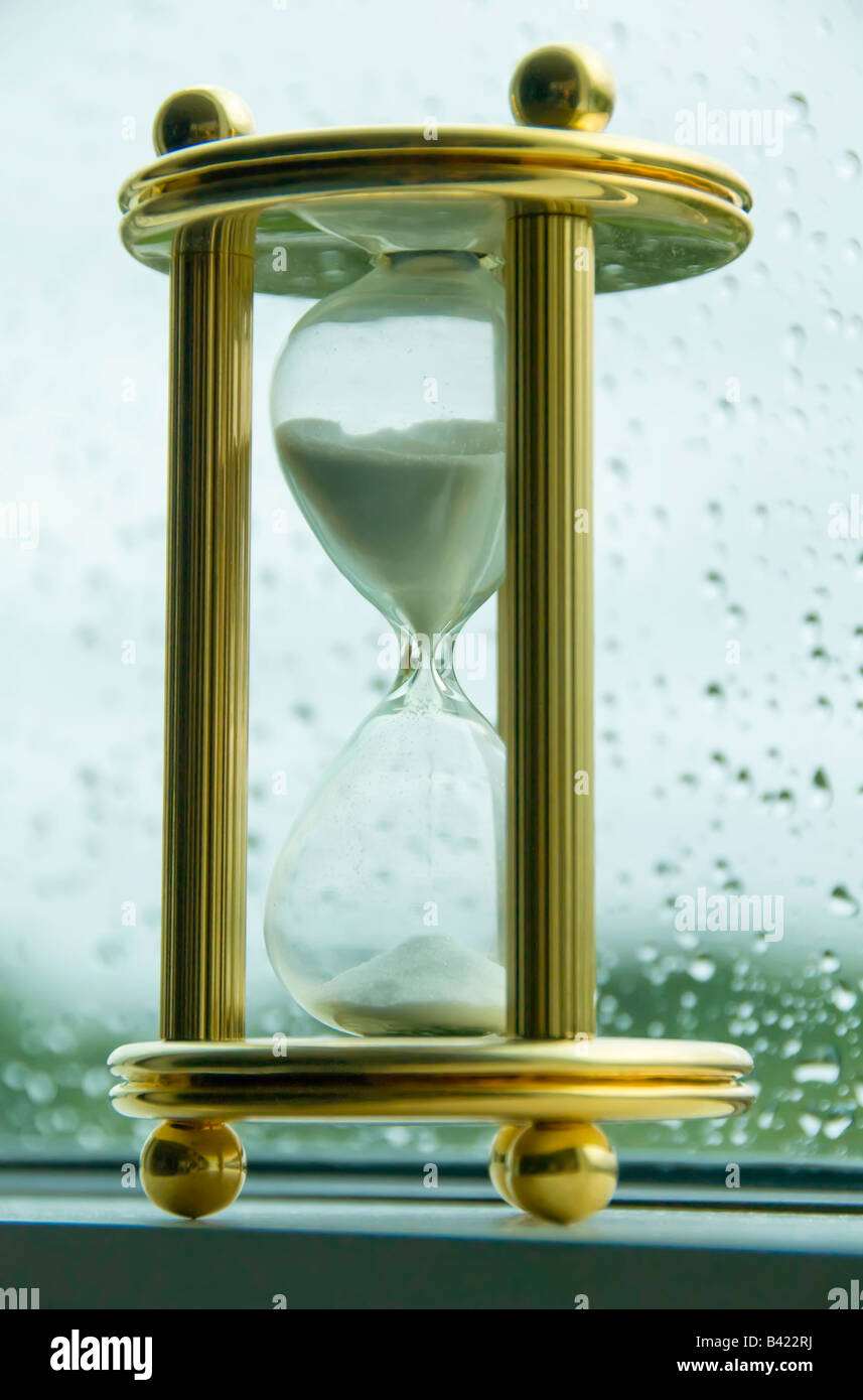 Hourglass on gold stand on ledge by rain spattered window Stock Photo ...