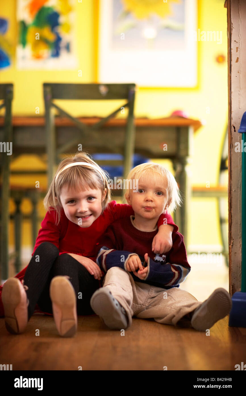 Two white children sit on the floor of their bright, colorful home ...
