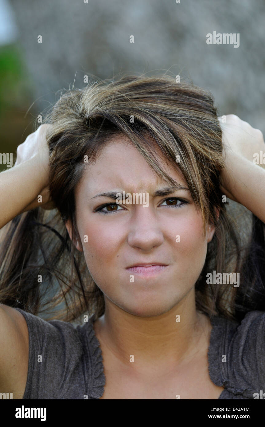A teenage girl clutches her hair with an angry expression on her face ...